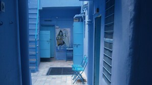 Uma ruela estreita com paredes e portas pintadas de azul, chão de azulejos e um mural em uma das paredes.