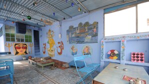Quarto com um mural, um ventilador, uma mesa e recipientes de sal, e uma janela.