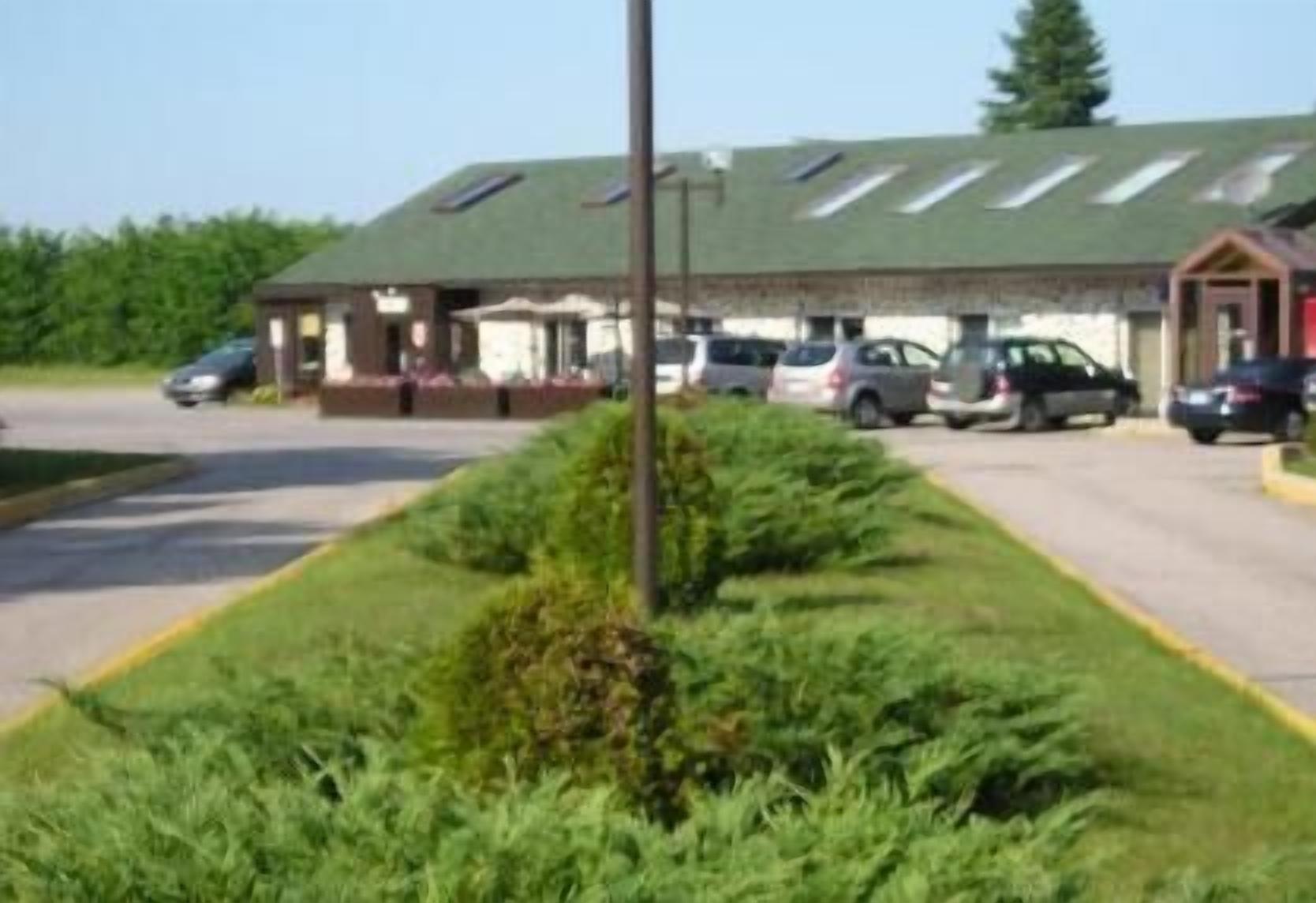 Um motel com telhado verde, estacionamento e uma pequena área de jardim.