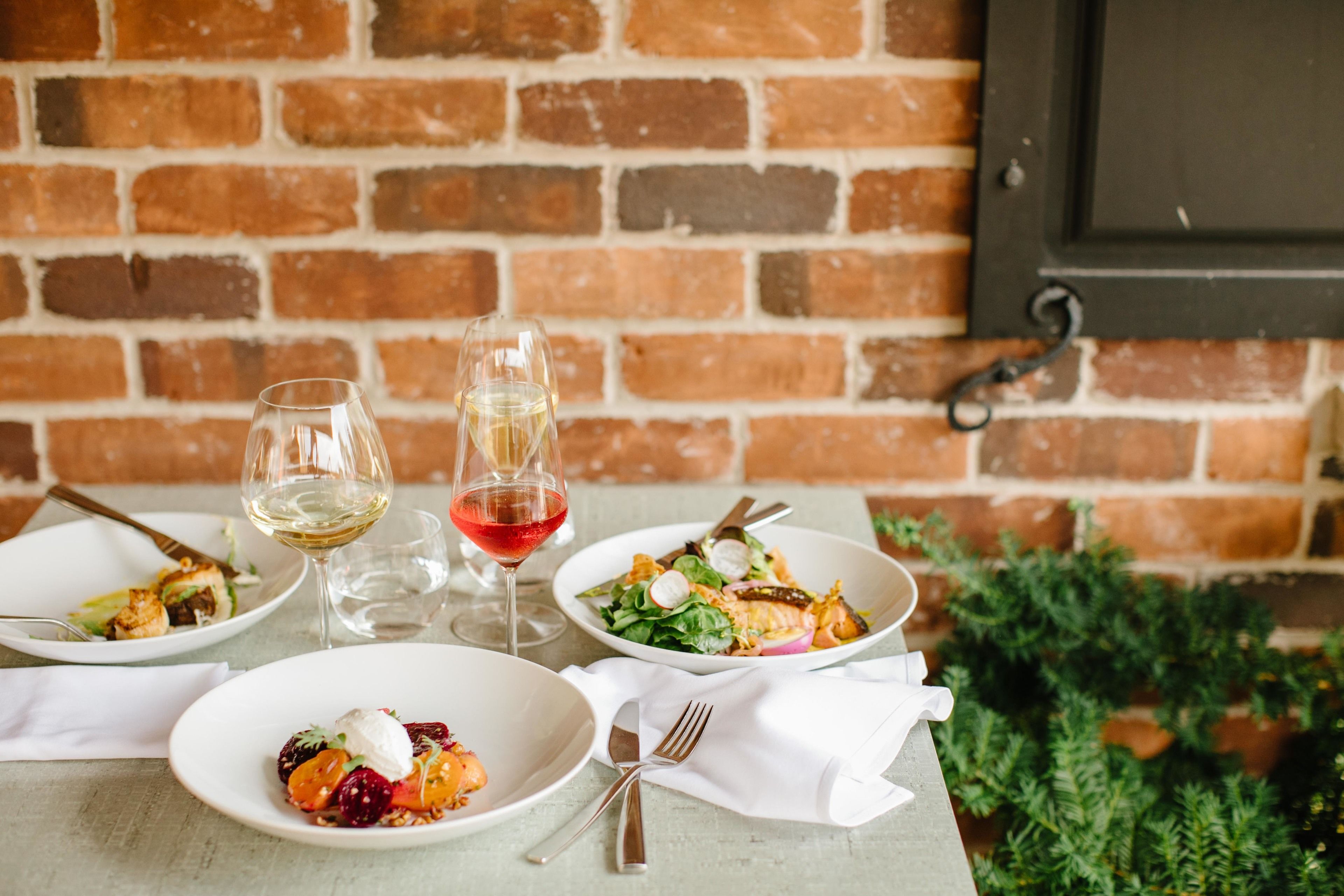 Uma mesa posta com pratos de comida, dois copos de vinho e talheres.