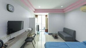 Quarto de hotel com televisão de tela plana, sofá, cama, poltrona e uma mesinha.