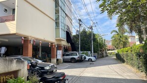 Um edifício com entrada coberta, escadaria e veículos estacionados.