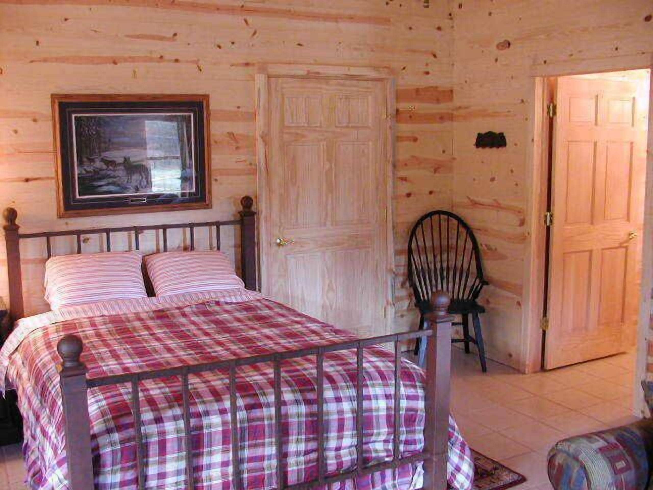 Quarto de cabana de madeira com cama, cadeira e porta.