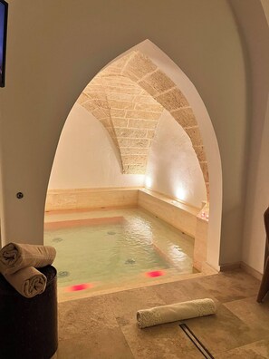 Um espaço de spa com um arco de pedra que dá para uma pequena piscina.