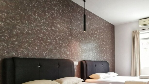 Quarto de hotel com duas camas, cabeceira escura, parede texturizada, luminária pendente e janela com cortinas.