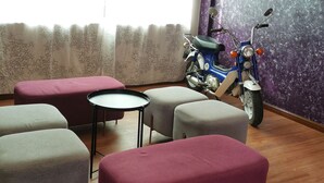 Um quarto com piso de madeira, uma scooter roxa e quatro pufes em cores variadas.