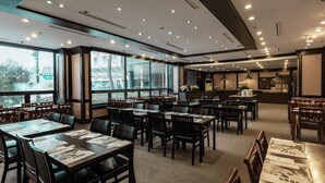 Um restaurante amplo com várias mesas e cadeiras, janelas grandes e um design de teto moderno.