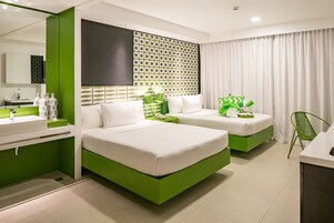 Quarto de hotel moderno com uma cama grande, área de estar separada, parede verde de destaque e um espelho grande.