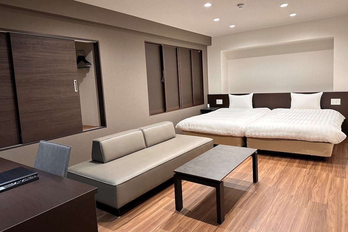 Quarto de hotel moderno com cama, sofá, mesa pequena e escrivaninha com controle remoto.