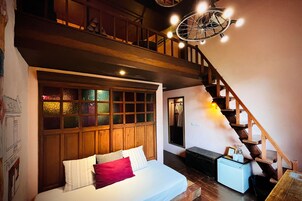 Quarto com cabeceira de madeira, cama com roupa de cama branca e listrada, cômoda azul pequena e escada com corrimãos de madeira.