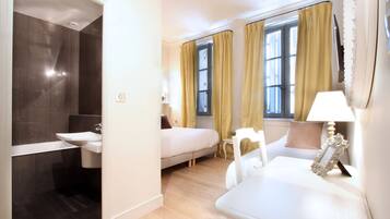 Quarto de hotel moderno com banheiro, cama, mesa de cabeceira e janela com cortinas.