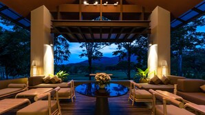 Uma área de estar moderna ao ar livre, com uma mesa redonda, assentos acolchoados e vista para uma paisagem natural.