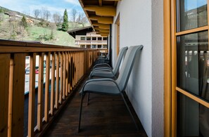 Uma varanda com guarda-corpo de madeira e uma fileira de cadeiras voltadas para um edifício com uma cruz no telhado.