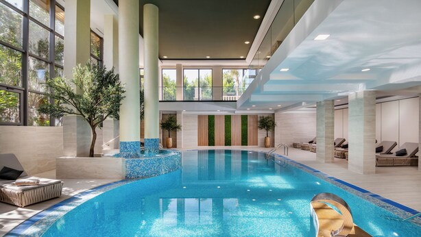 Piscina interior com água cristalina, rodeada por espreguiçadeiras e um pequeno cascata.