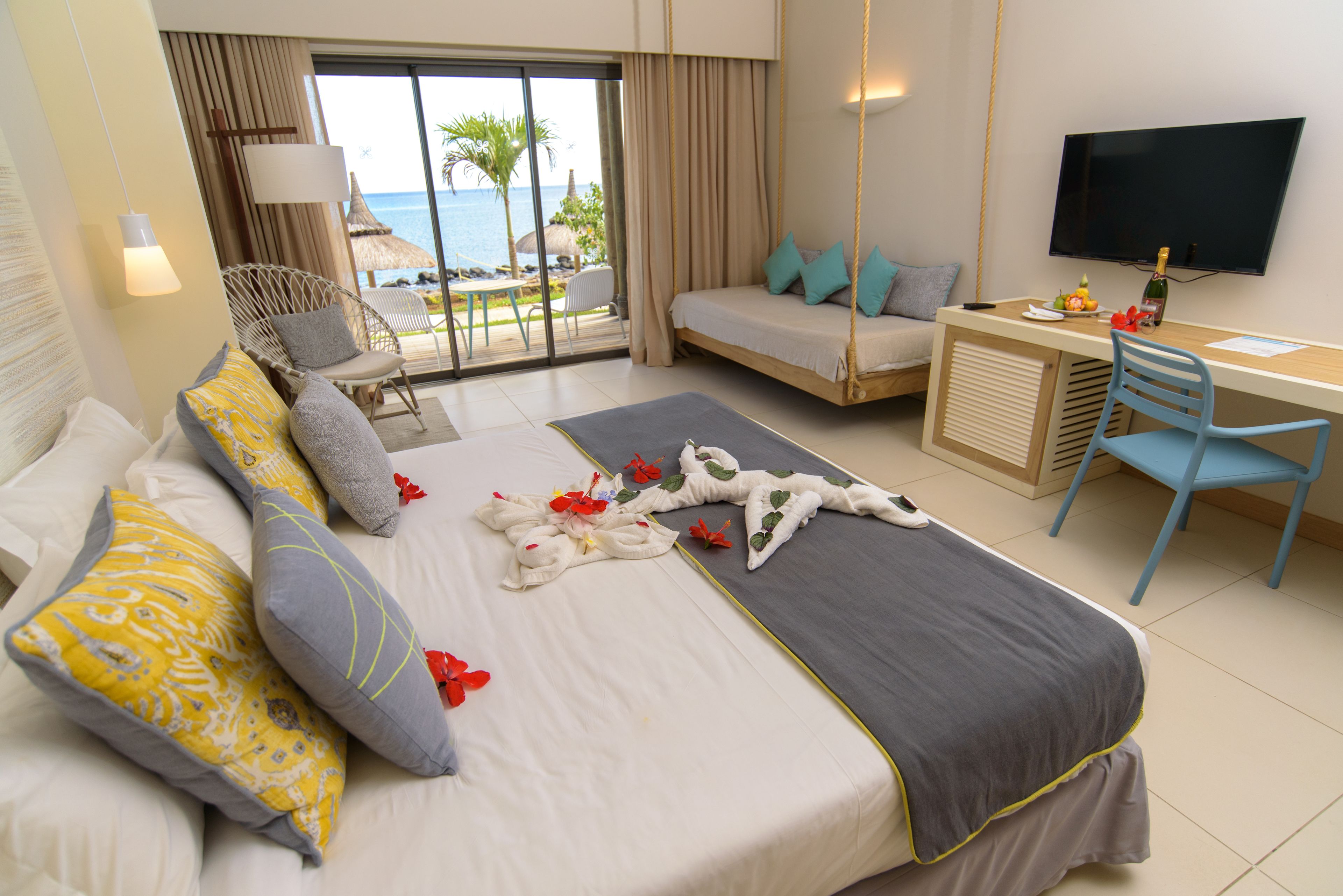 Quarto de hotel com cama, escrivaninha, televisão e vista para o mar.