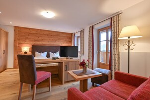 Um quarto aconchegante com uma escrivaninha de madeira, uma cama com televisão, uma cadeira, um sofá vermelho e um abajur.