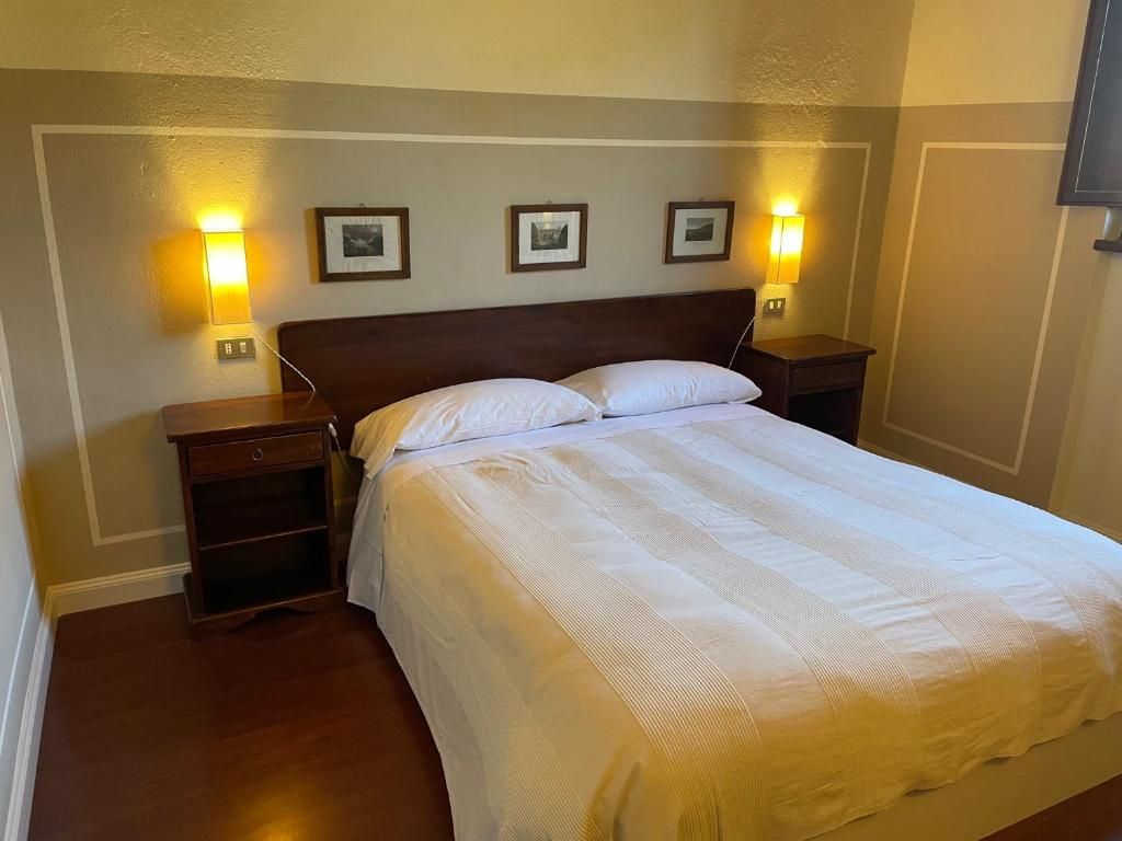 Quarto de hotel com uma cama grande, duas mesas de cabeceira e luminárias fixadas na parede.