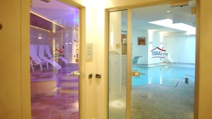 Um saguão de hotel com porta de vidro que dá para uma área de piscina, uma mesa de recepção e cadeiras de lounge.