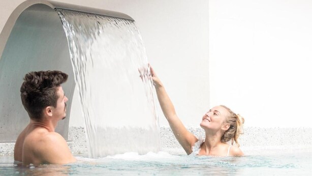 Um casal em uma piscina com uma cascata.