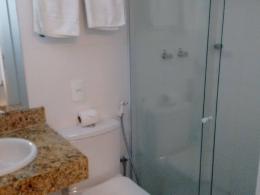 Casa de banho com lavatório bancada em granito, sanita e cabine de duche em vidro.