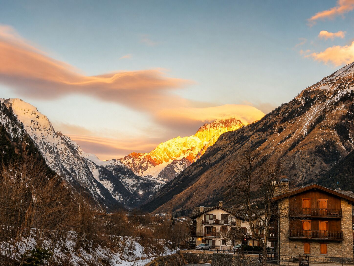 Um refúgio de montanha com fachada de pedra, várias varandas e vista para picos nevados.