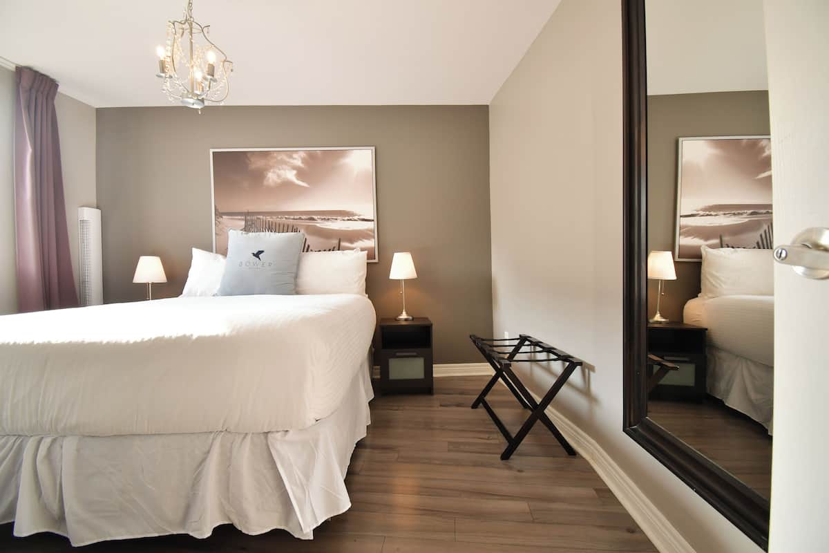 Quarto de hotel com uma cama grande, duas mesas de cabeceira, um abajur, uma mesinha e um espelho amplo.