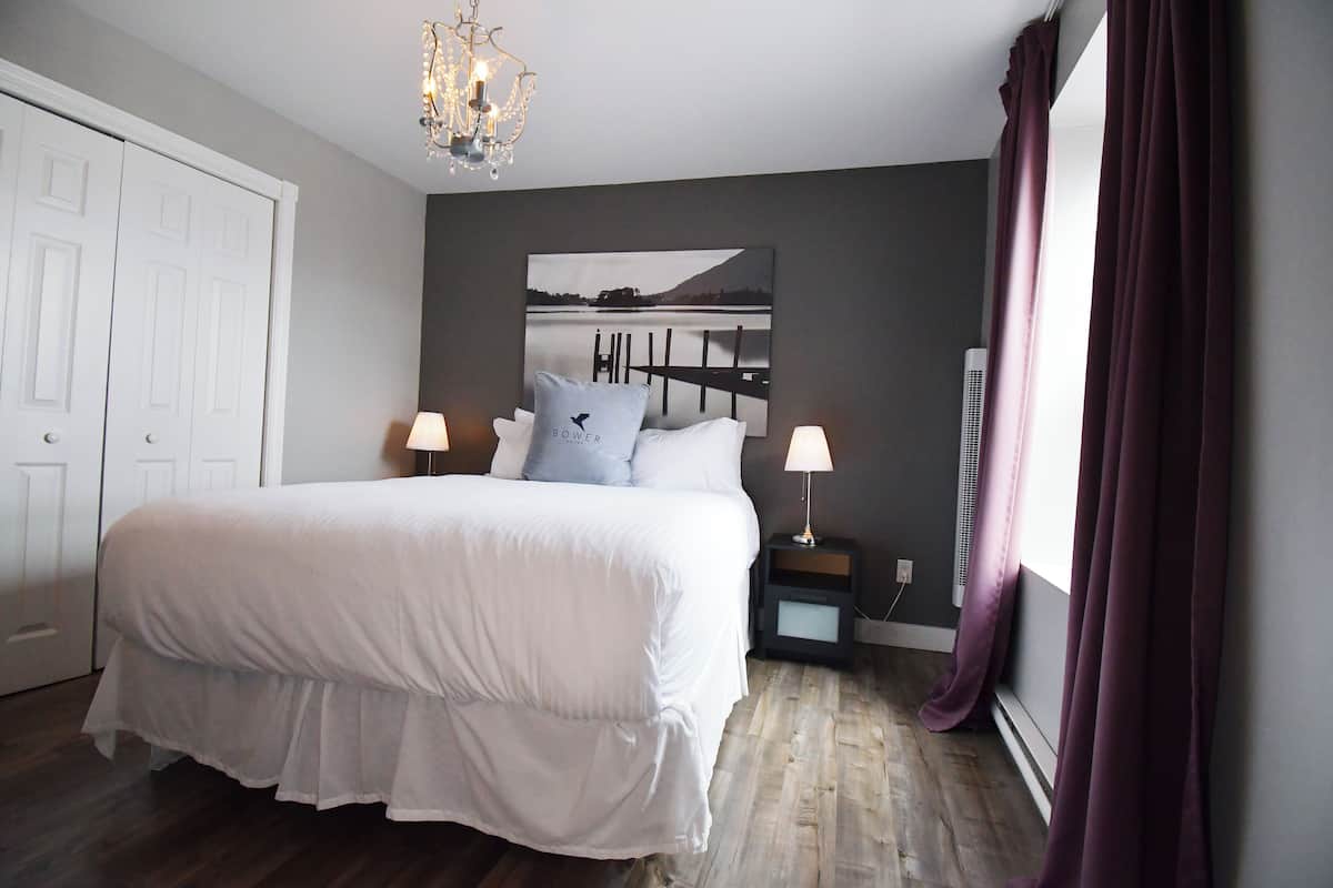 Quarto com uma cama grande, duas mesas de cabeceira com luminárias, um candelabro, uma janela com cortinas e um quadro na parede.