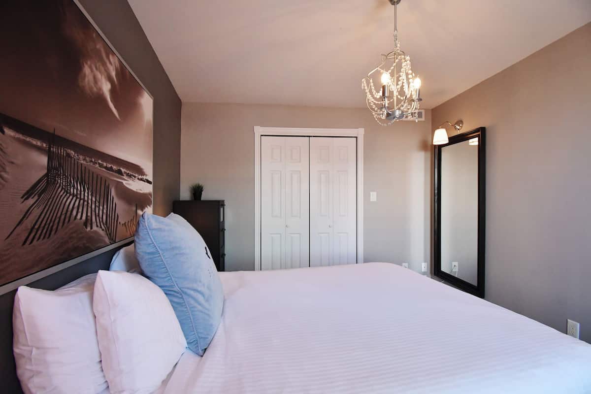 Quarto com cama, lustre, guarda-roupa e espelho.