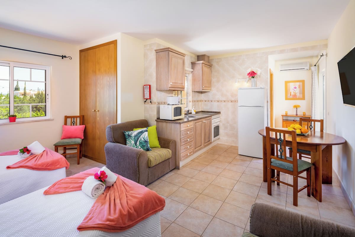 Quarto de hotel com duas camas, cozinha compacta, espaço para refeições e banheiro.