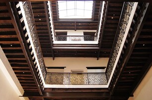 Interior com vários níveis, vigas de madeira e grades de metal detalhadas.