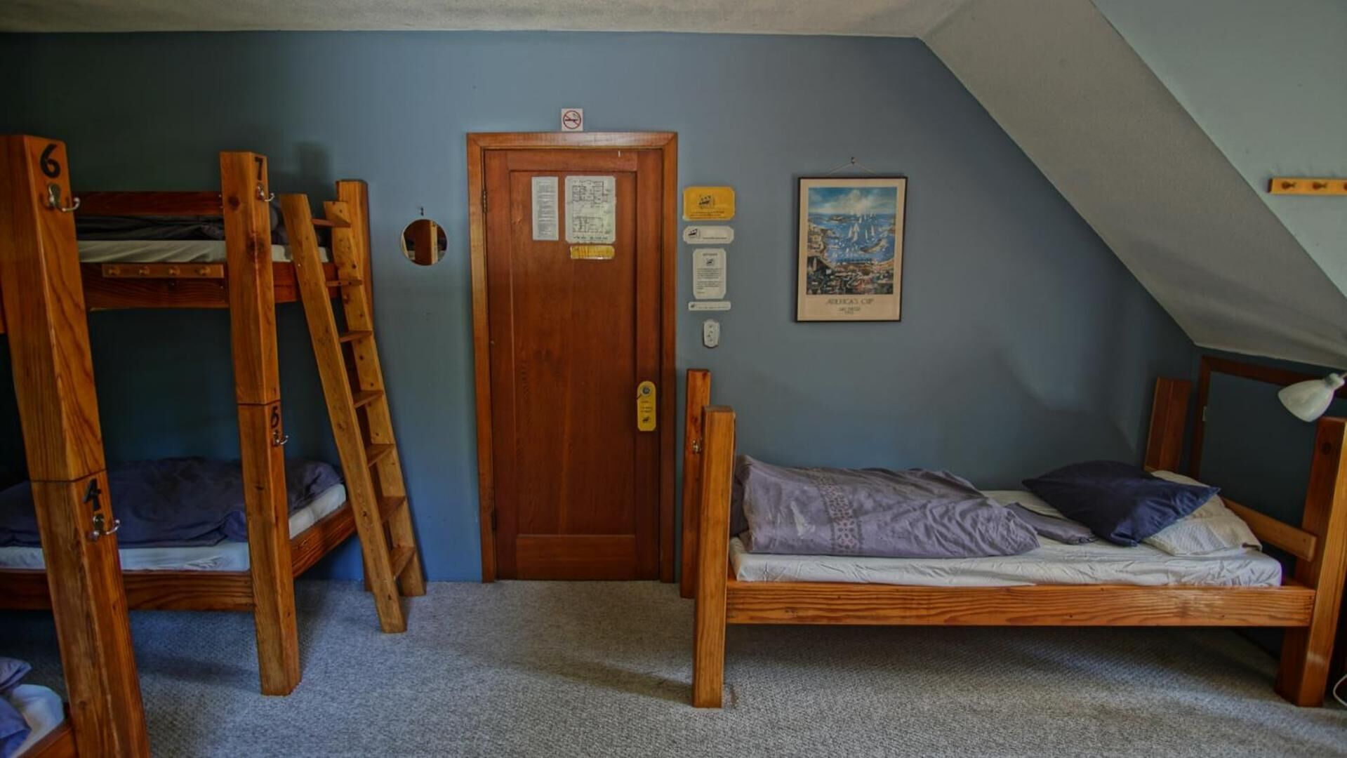 Quarto em dormitório com beliches, uma porta com aviso, um quadro emoldurado e uma luminária.
