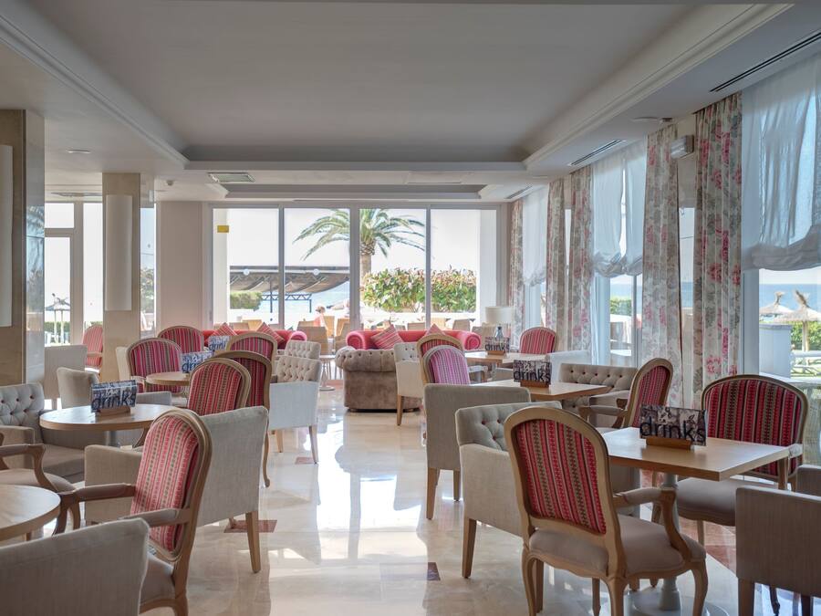 Um amplo hall de hotel com várias áreas de estar, incluindo sofás e cadeiras, dispostas ao redor de mesas. Grandes janelas oferecem vista para o exterior.