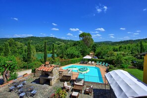 Uma área de piscina com espreguiçadeiras e guarda-sóis, rodeada por vegetação e colinas.