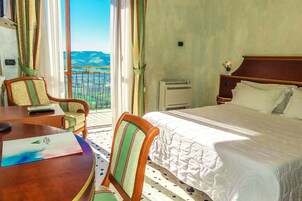 Quarto de hotel com cama, escrivaninha, cadeira e vista para o exterior.