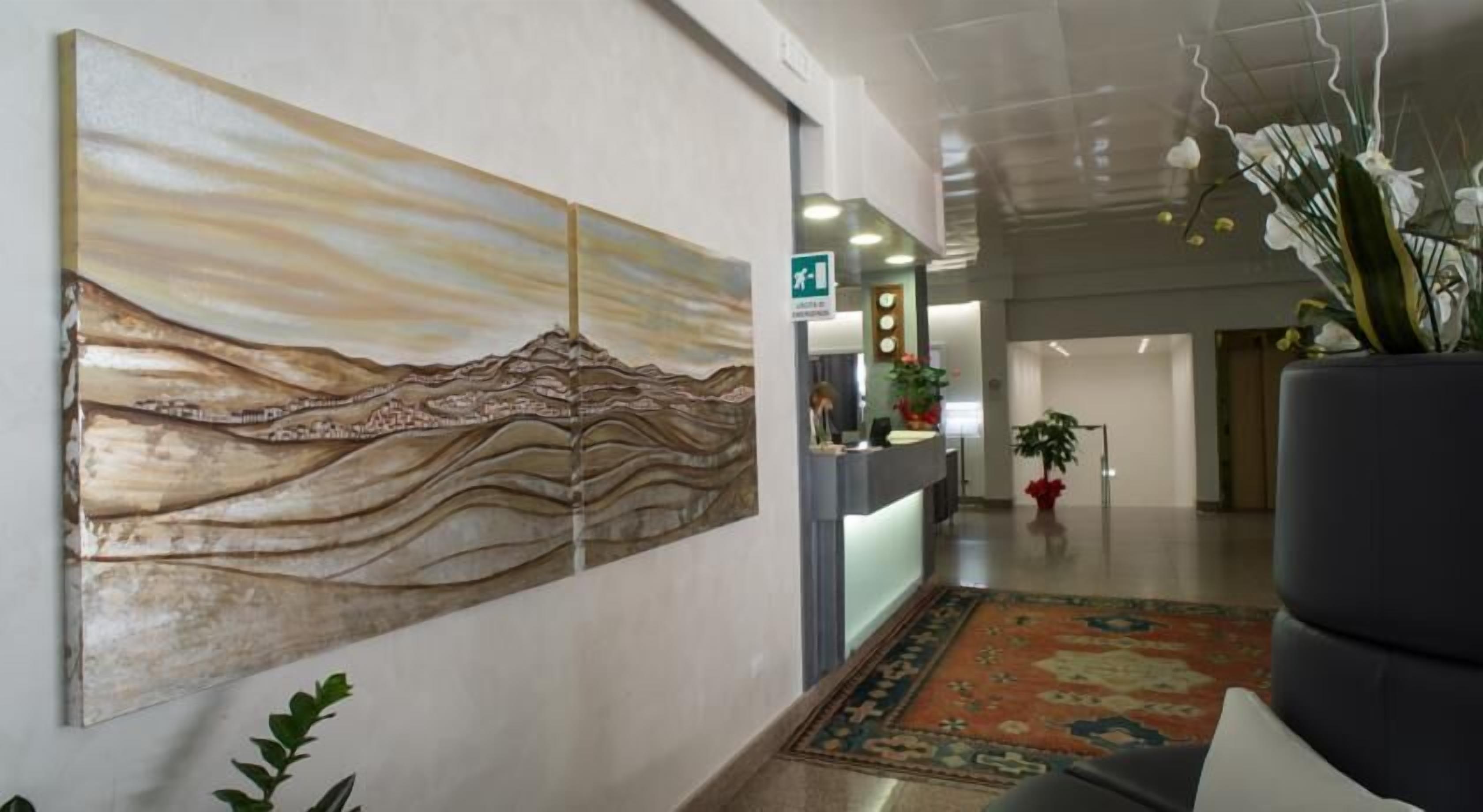 Uma área de recepção com uma grande pintura abstrata, um balcão de recepção, um vaso de planta e um tapete estampado.
