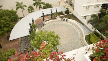 Um pátio circular com uma fonte central, rodeado por palmeiras e plantas em vasos.