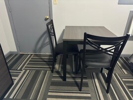 Quarto com carpete cinza, parede cinza e mesa de madeira com duas cadeiras.