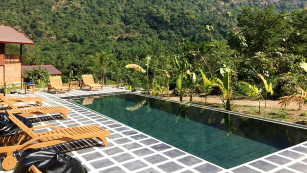 Piscina infinita com espreguiçadeiras de madeira e um pequeno edifício ao fundo.