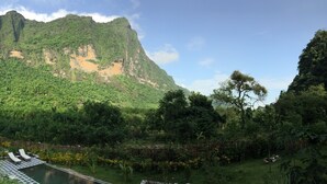 Uma área de piscina com espreguiçadeiras, rodeada por vegetação exuberante e com montanhas ao fundo.