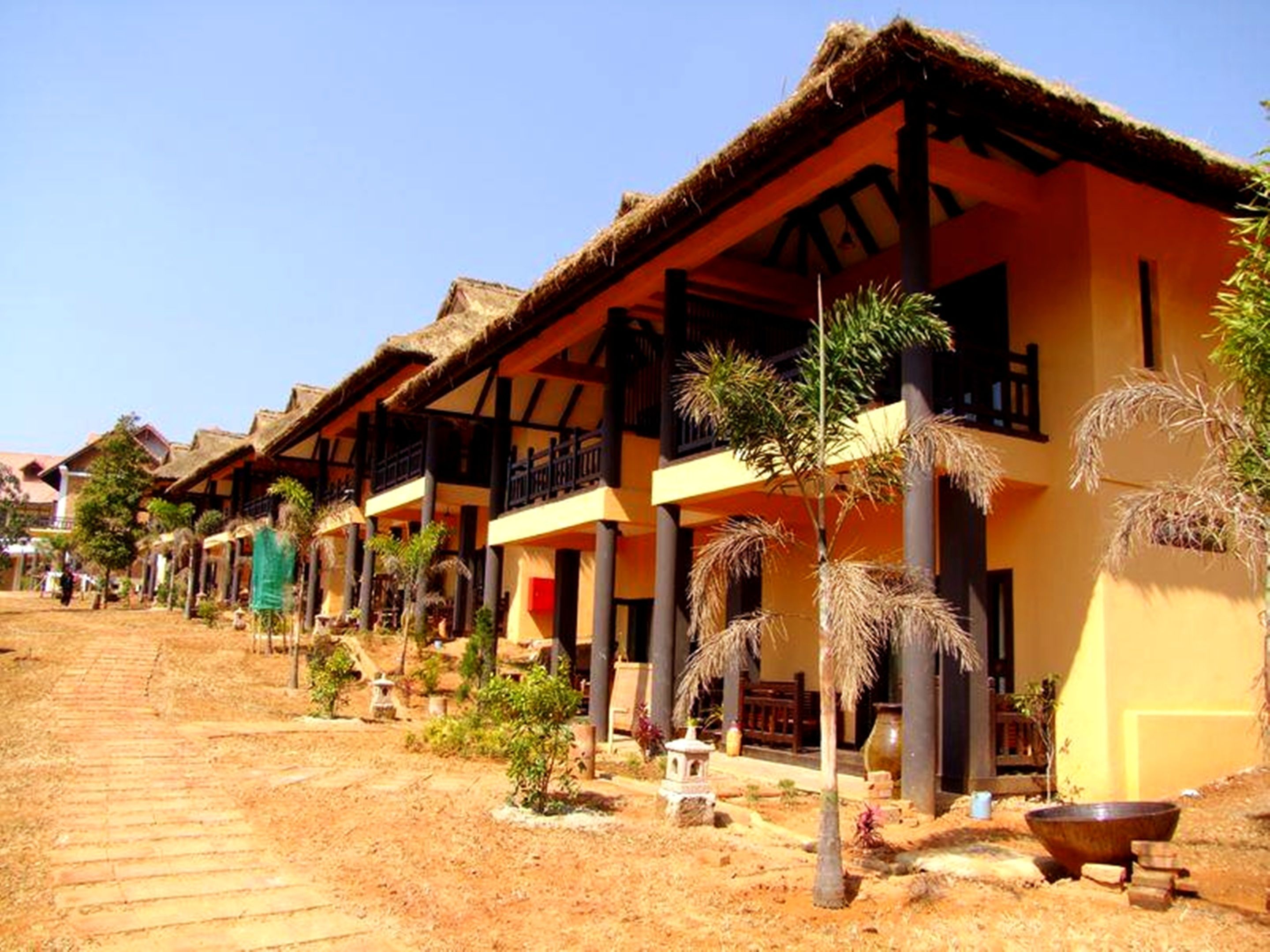 Uma fileira de edifícios em estilo tradicional com telhados de palha, varandas e um calçada pavimentada.