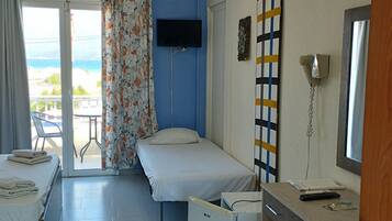 Quarto de hotel pequeno com cama, escrivaninha, cadeira, televisão e vista para o mar.