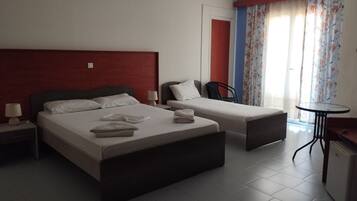 Quarto de hotel com duas camas, uma mesinha, uma cadeira e mesa de cabeceira com abajur.