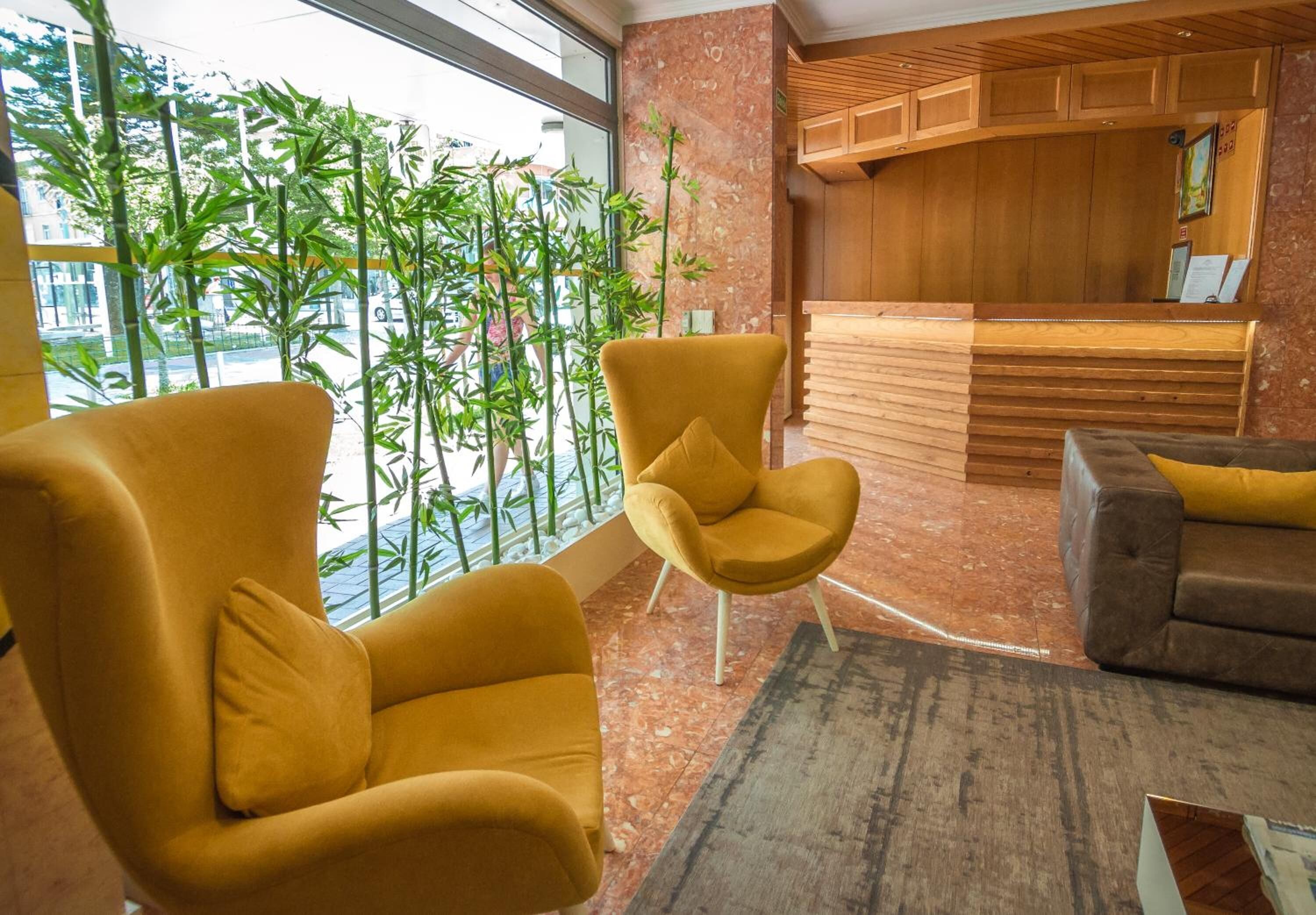 Um hall moderno com balcão de recepção, poltronas amarelas e vista para bambus.