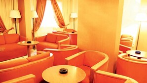 Quarto de hotel com mobiliário laranja, incluindo sofás e poltronas, dispostos em torno de uma mesa central.
