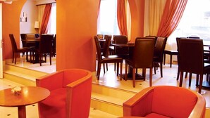 Um hall de hotel com área de refeições, cadeiras vermelhas e um lustre.