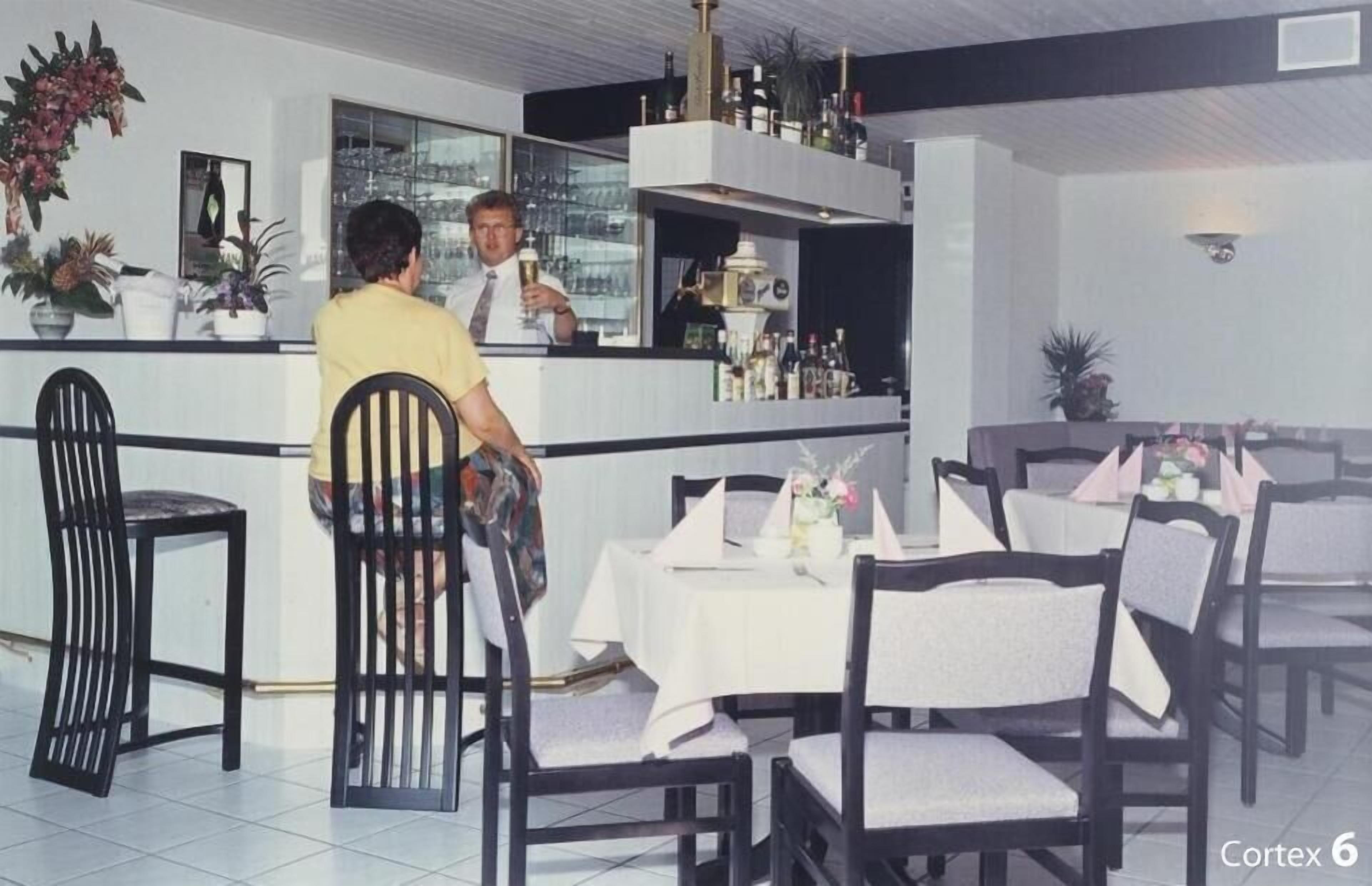 Uma área de bar moderna com balcão, banquetas e um espaço de refeições com mesas e cadeiras.