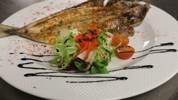 Um prato branco com peixe grelhado, salada e tomate.