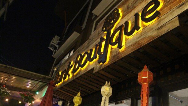 Uma placa de madeira com letras iluminadas que formam a palavra 'boutique' sobre um fundo escuro.