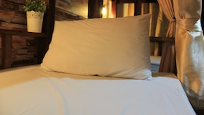 Uma cama com roupa de cama branca, uma planta pendurada e vigas de madeira.