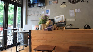 Interior acolhedor de café com um balcão de madeira, um laptop, um relógio e uma parede decorada com diversos sinais e um mapa.